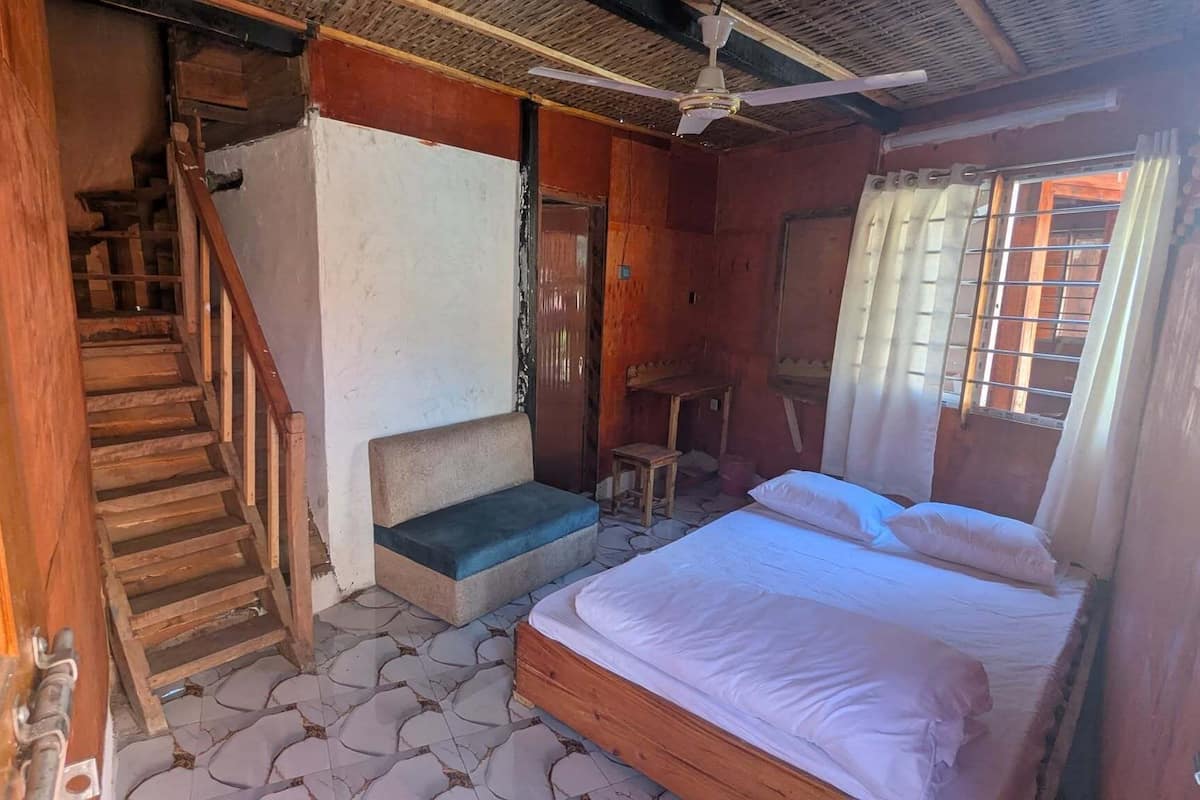 Quarto com escada de madeira, cama com roupa de cama branca, uma mesinha e uma janela com cortinas.