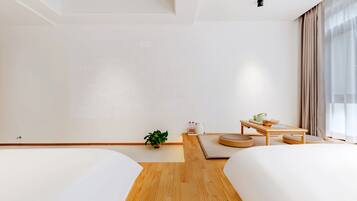 Quarto de hotel moderno com chão de madeira, duas camas, uma mesinha com uma planta e uma janela com cortinas.