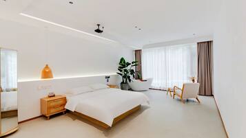 Quarto de hotel moderno com uma cama grande, mesa de cabeceira, cadeira, planta em vaso e uma janela ampla com cortinas.