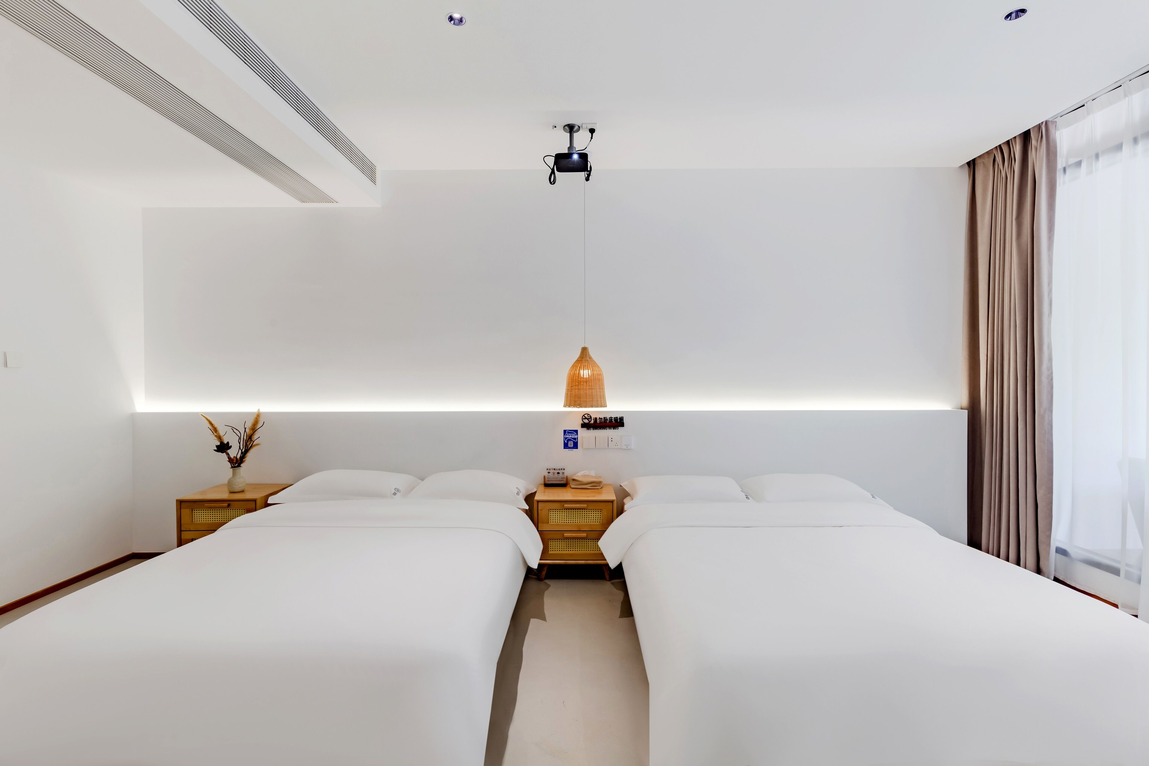 Quarto de hotel com duas camas, uma mesa de cabeceira com abajur e ar condicionado no teto.