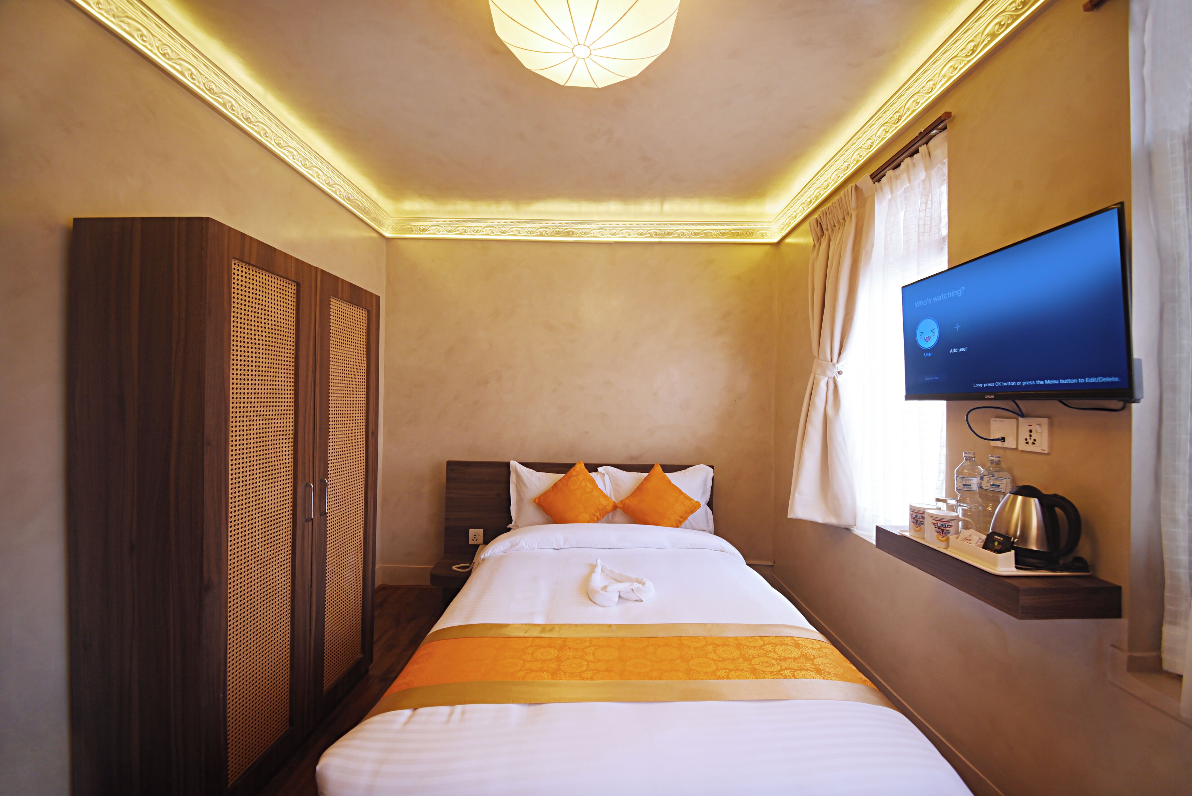 Quarto de hotel com cama, televisão, guarda-roupa e prateleira com artigos de higiene pessoal.