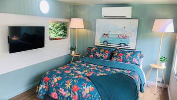 Quarto com cama, duas mesas de cabeceira, televisão, ar condicionado e janela com vista para o verde.