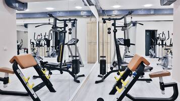 Academia com paredes espelhadas, equipamentos de ginástica e piso de madeira.