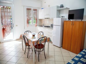 Uma cozinha compacta com uma mesa de jantar, cadeiras, geladeira, micro-ondas e um armário de madeira.