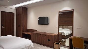 Quarto de hotel moderno com uma cama, escrivaninha, televisão e um espelho grande.