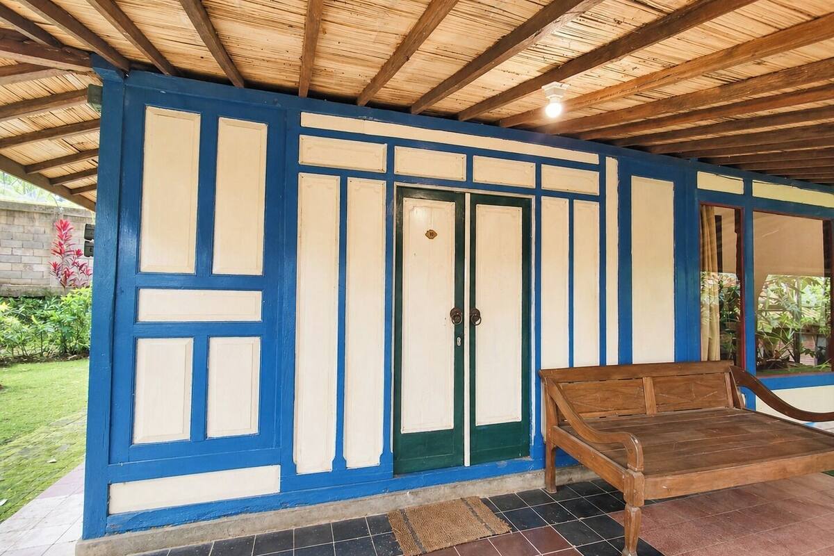 Um quarto com teto de madeira, parede azul e branca, um banco de madeira e piso de azulejos.