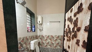 Um banheiro pequeno com vaso sanitário, chuveiro e secador de mãos. Há uma janela com vista para o exterior, e uma parede decorativa com padrão floral.