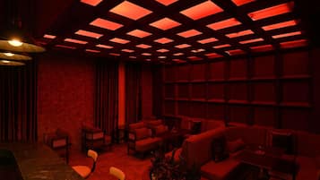 Um espaço com iluminação suave e tons avermelhados, com área de bar, sofás e cadeiras para acomodação, e parede com padrão decorativo.
