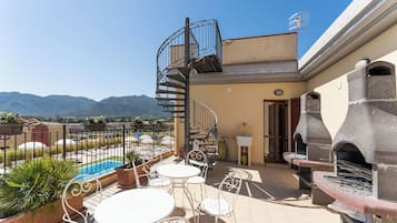 Terraço no telhado com área de estar ao ar livre, escada em espiral, churrasqueira de pedra e vista para montanhas.