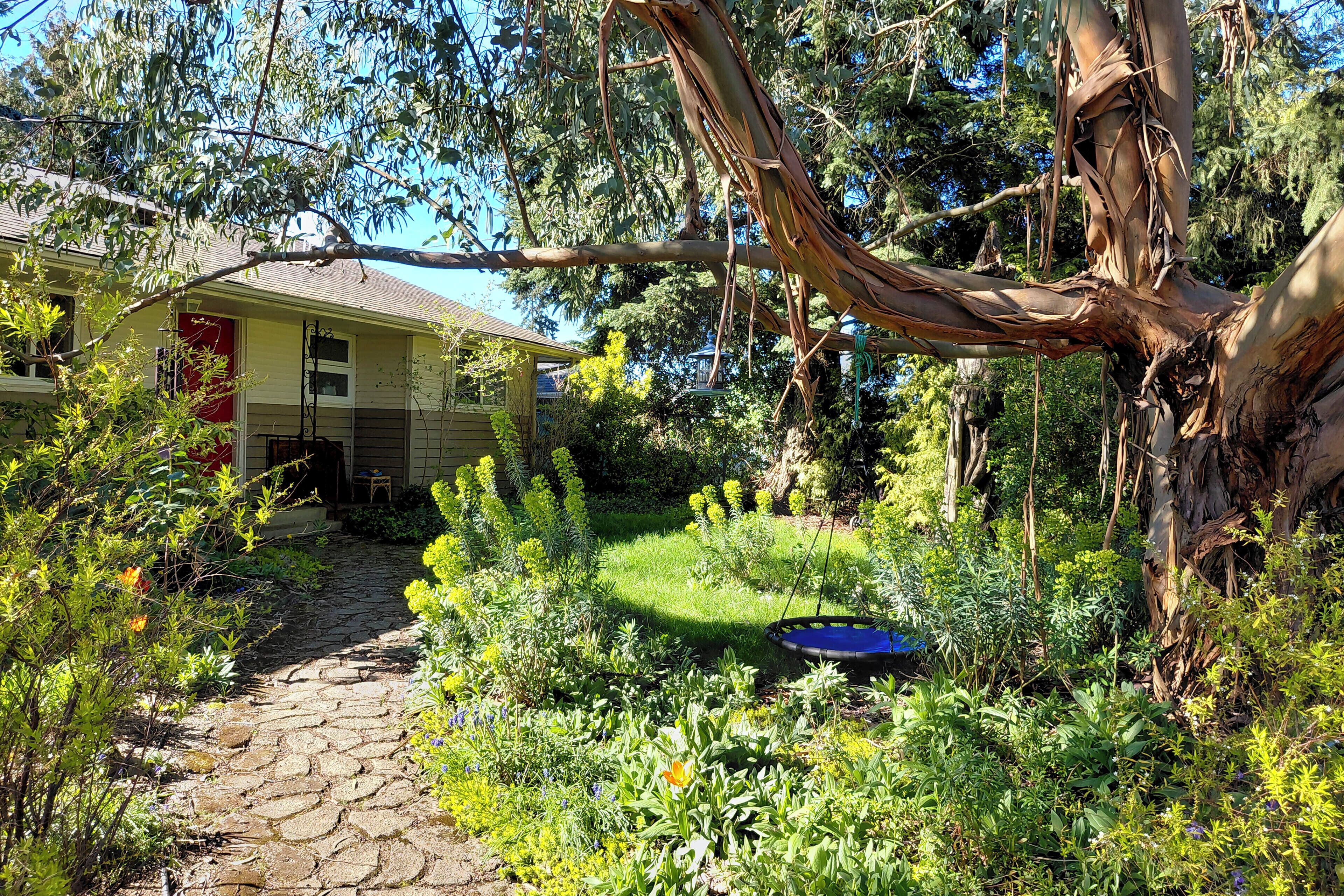 Um jardim com um caminho de pedra, um balanço e uma casa com porta vermelha.