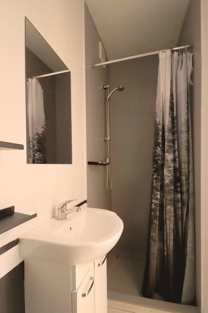 Casa de banho com lavatório branco, espelho e chuveiro com cortina.