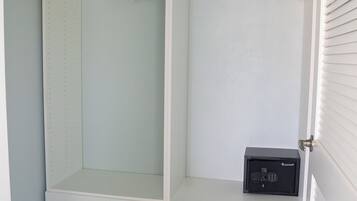Um closet amplo e branco com prateleiras, barra para pendurar roupas, um cofre pequeno e piso revestido com azulejos.