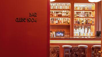 Uma área de bar com prateleiras cheias de garrafas e uma placa com a inscrição 'BAR CLUBE 1904'.