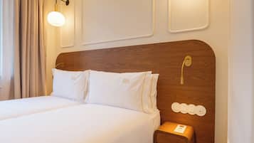 Quarto de hotel com cabeceira de madeira, duas almofadas brancas, mesa de cabeceira e luminárias fixadas na parede.
