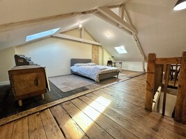 Quarto com teto inclinado, uma cama, escrivaninha e uma cadeira.