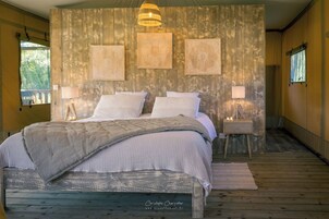 Quarto com piso de madeira, cama com roupa de cama branca, duas mesas de cabeceira com abajures e três decorações emolduradas na parede.