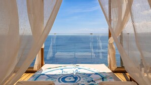 Quarto com cama de frente para uma janela grande com vista para o mar.