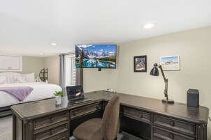 Quarto de hotel com cama, escrivaninha com laptop, televisão na parede e abajur.