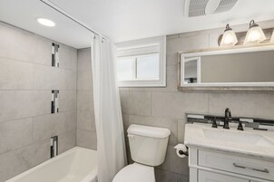 Uma casa de banho moderna com banheira, sanita e toucador com espelho.