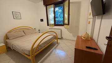 Um quarto com cama, mesa de cabeceira, cômoda de madeira, televisão e janela com cortinas.