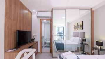 Quarto de hotel com cama, mesas de cabeceira, televisão, banheiro com vaso sanitário e pia, e porta de correr para uma varanda.