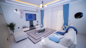 Uma sala de estar moderna com sofá, puf, mesa de centro e TV na parede.