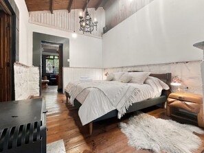 Quarto com uma cama grande, piso de madeira, um candelabro e uma parede de pedra.