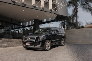 Um Cadillac SUV preto estacionado em frente a um edifício moderno com grandes janelas e uma parede de tijolos.