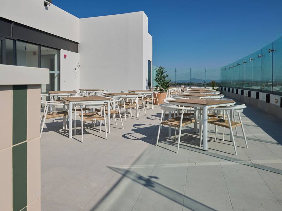 Um terraço ao ar livre com mesas e cadeiras, um vaso de planta e vista para a cidade.