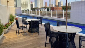Uma área de piscina no terraço com vista para o horizonte da cidade, incluindo uma torre de comunicação alta.