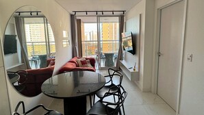 Uma sala de estar moderna com uma mesa de jantar redonda, cadeiras pretas, um sofá vermelho e uma janela grande com vista para edifícios altos.