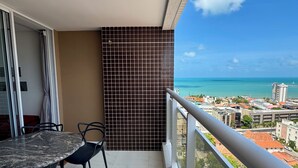 Uma varanda com uma mesa de jantar e cadeiras, um muro de azulejos e vista para o mar e a paisagem urbana.