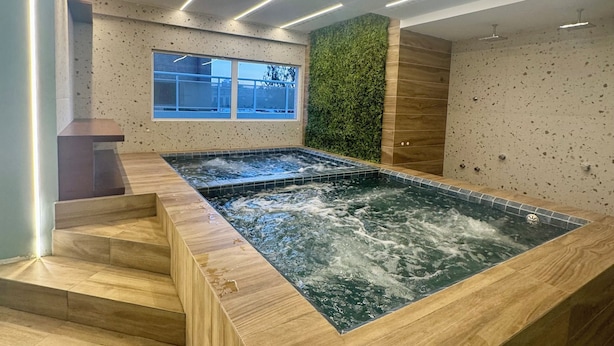 Uma área de spa com duas banheiras de hidromassagem, degraus de madeira, uma janela e uma parede verde.