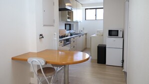 Uma cozinha compacta com mesa de madeira, armários brancos, micro-ondas e geladeira compacta.