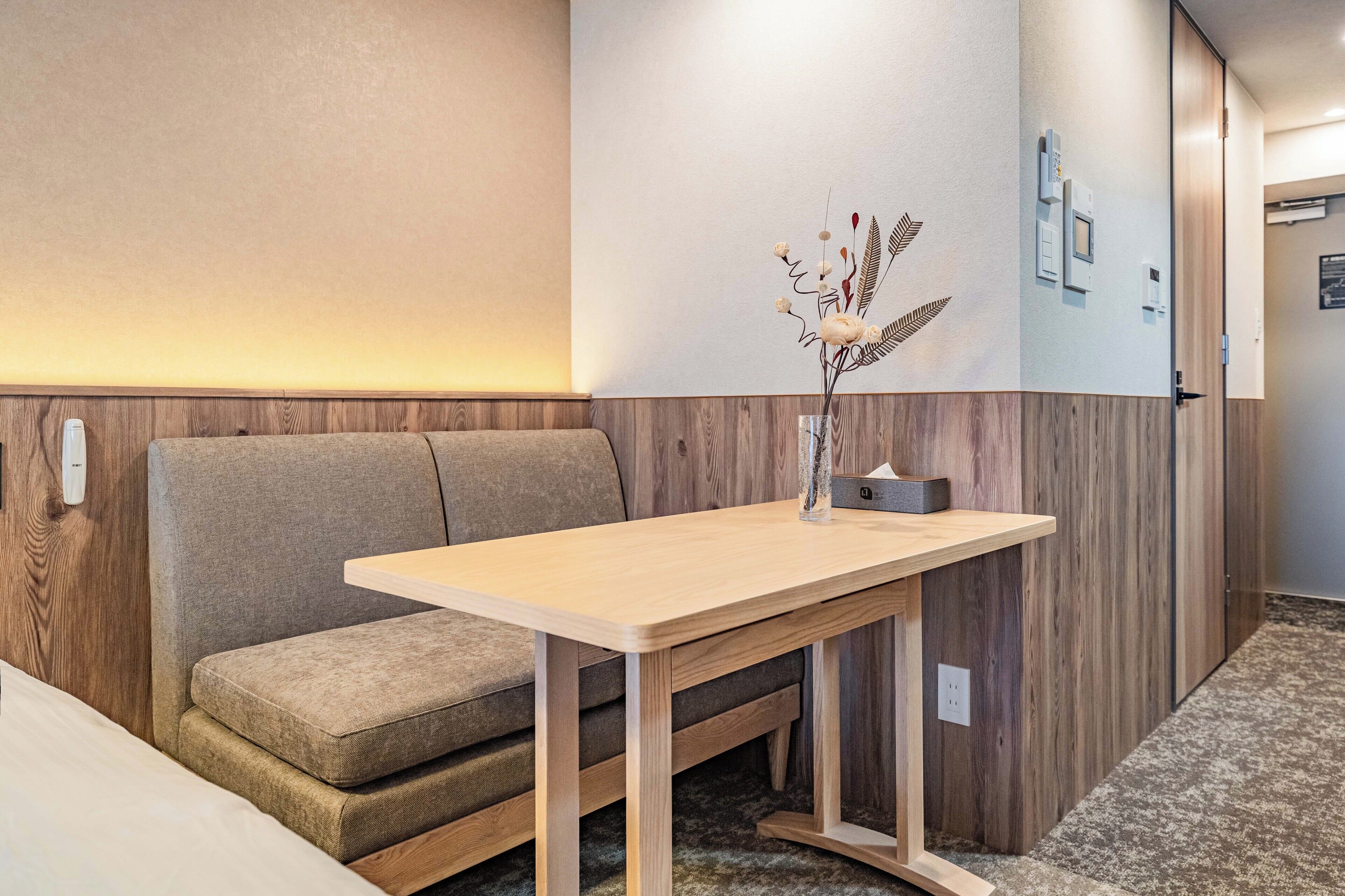 Quarto de hotel moderno com um banco de madeira, uma pequena mesa e uma peça decorativa na parede.