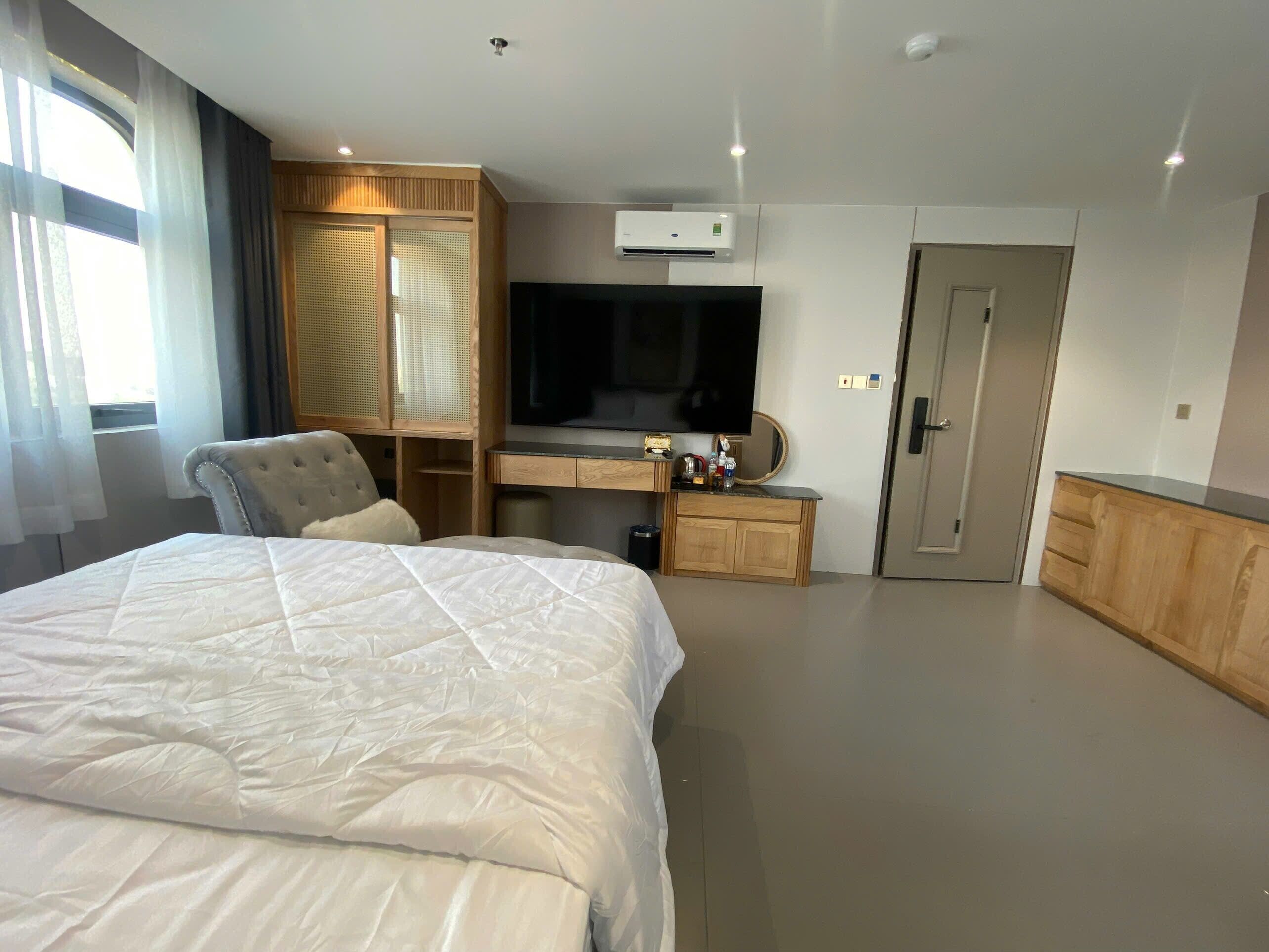 Quarto de hotel com uma cama grande, uma escrivaninha com televisão de tela plana, um guarda-roupa e uma porta.