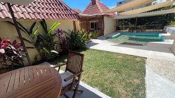 Área de pátio com piscina, mesa de madeira e uma cadeira.