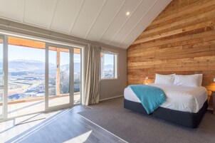 Quarto com uma cama grande, paredes de madeira e vista para uma paisagem nevada através de grandes janelas.