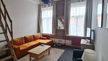 Uma sala de estar com escada de madeira, sofá modular, mesa de centro, poltrona estampada e luminária.