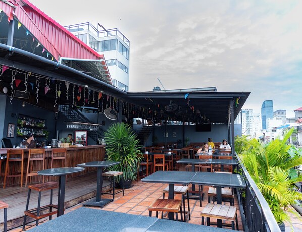 Uma área externa com mesas, cadeiras, um bar e vista para o horizonte da cidade.