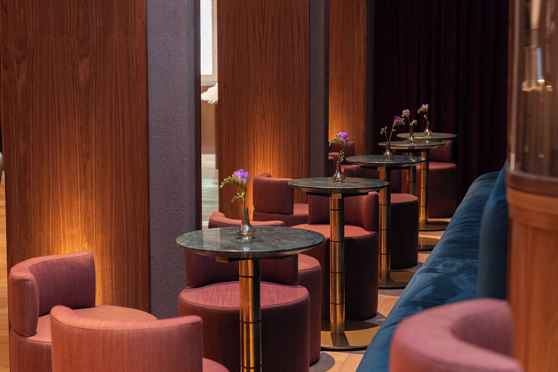 Um lobby de hotel com mesas redondas, cadeiras estofadas vermelhas e um sofá azul.