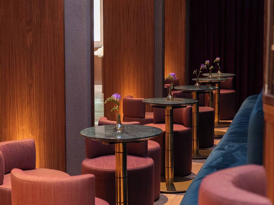 Um lobby de hotel com mesas redondas, cadeiras estofadas vermelhas e um sofá azul.