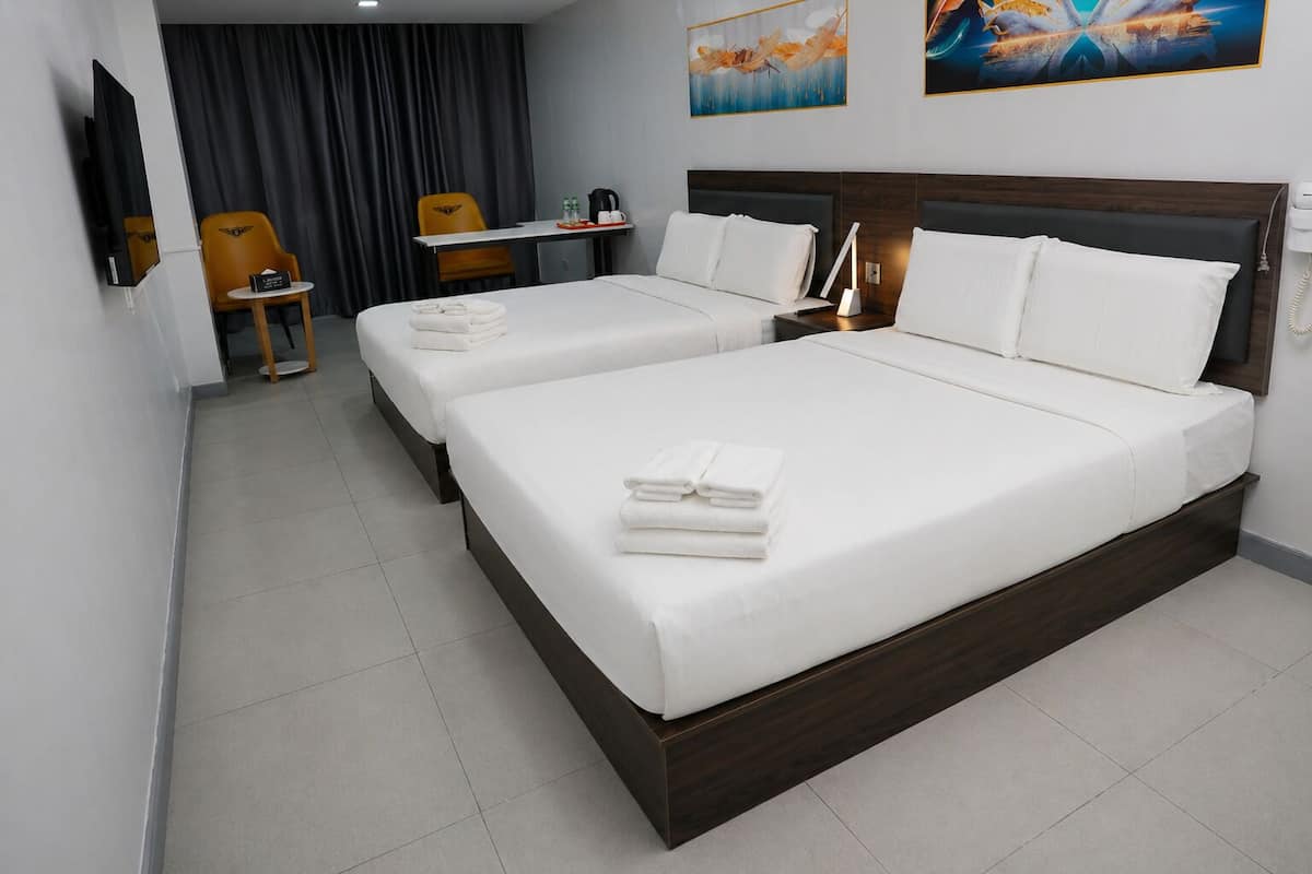 Quarto de hotel com duas camas, uma escrivaninha, uma cadeira e obras de arte nas paredes.