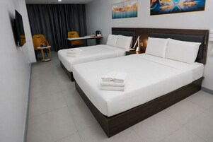Quarto de hotel com duas camas, uma escrivaninha, uma cadeira e obras de arte nas paredes.