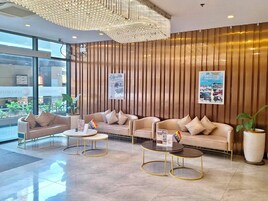 Um lobby de hotel com uma mesa de recepção, dois sofás, um candelabro e uma grande planta em vaso.