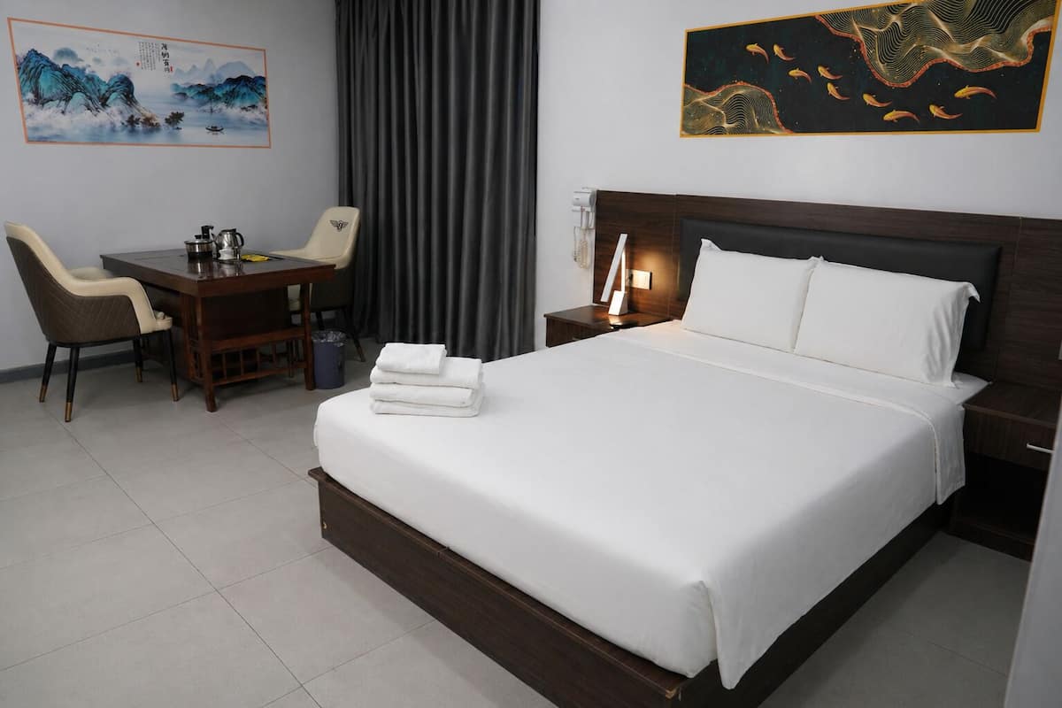Quarto de hotel com cama, escrivaninha com cadeira, mesa com cadeira, mesa de cabeceira e obras de arte nas paredes.
