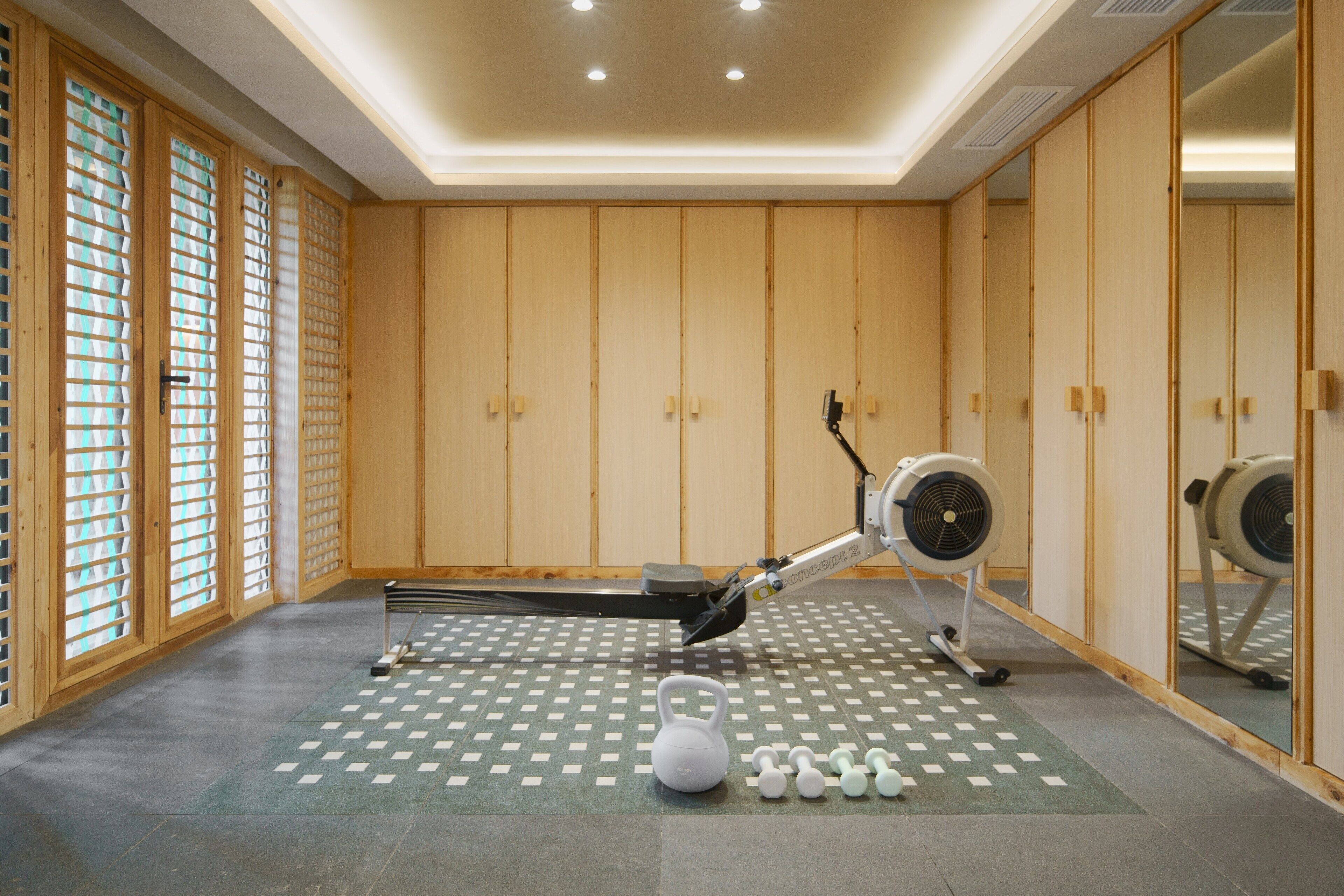 Quarto com piso de tatame, ventilador de teto e equipamentos de exercícios, incluindo um kettlebell e halteres.