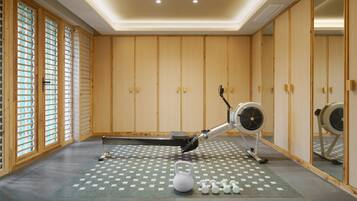 Quarto com piso de tatame, ventilador de teto e equipamentos de exercícios, incluindo um kettlebell e halteres.