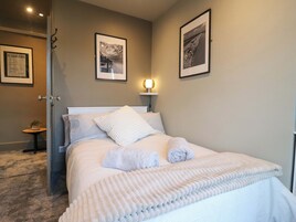 Cama bem arrumada com roupa de cama listrada e toalhas dobradas, uma pequena mesa de cabeceira com abajur, e duas fotos emolduradas na parede.