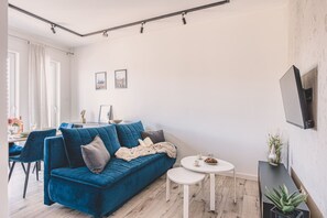 Uma sala de estar moderna com um sofá azul, uma mesa redonda pequena e uma TV fixada na parede.